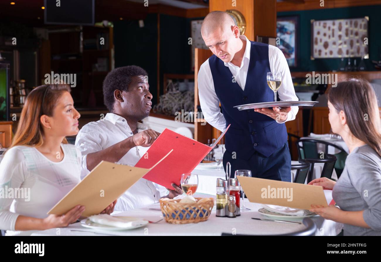 Polite waiter helping guests in choosing meals from menu Stock Photo ...