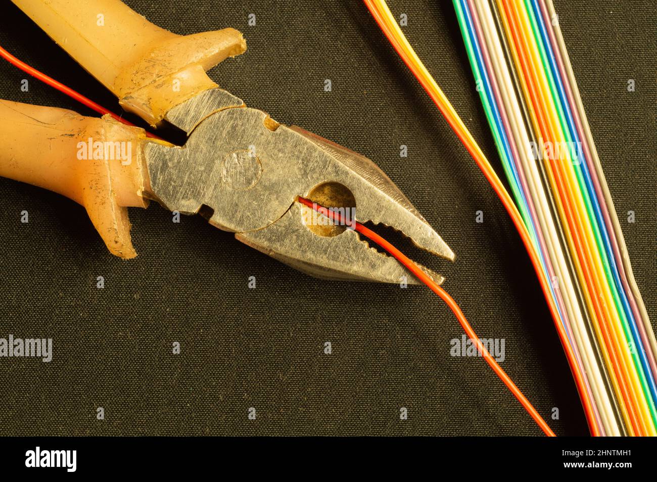 Pliers cuts a red wire on black background. pliers with orange handles ...