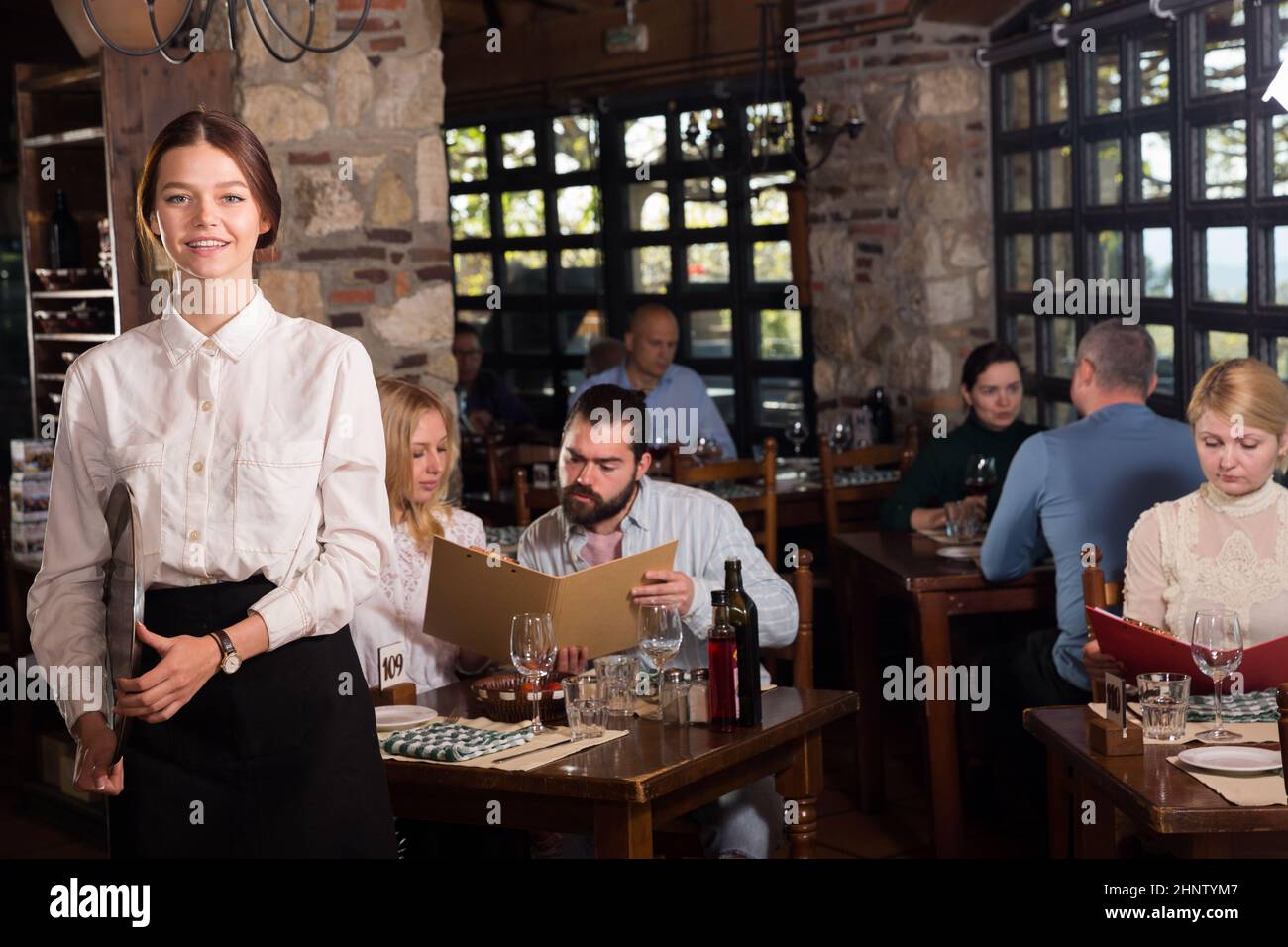 Professional waitress greeting customers at table in rustic restaurant ...