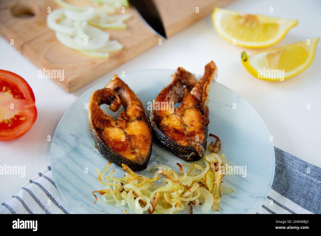 Fried fish with onions is on a plate, on a waffle towel, next to it is ...