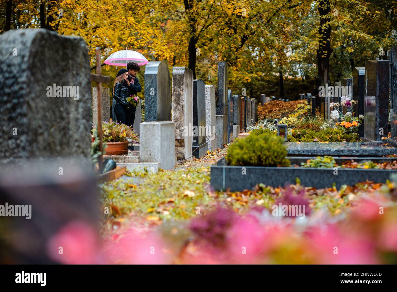 Graves on cemetery in autumn with a couple mourning the dead standing ...