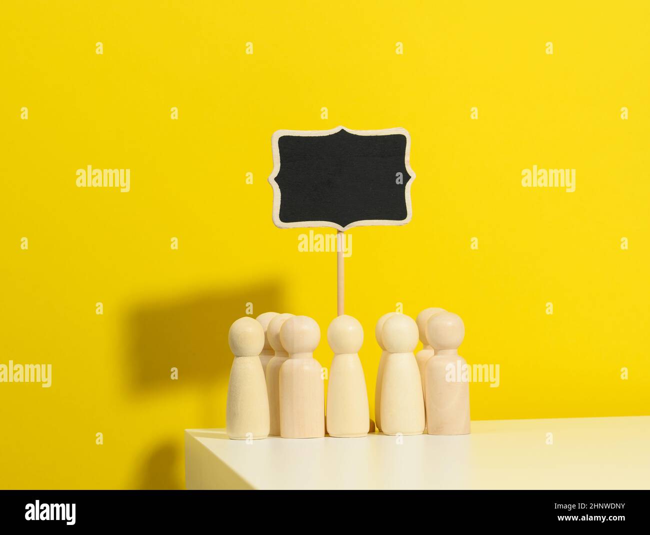 group of wooden figurines and a blank signpost on a yellow background ...