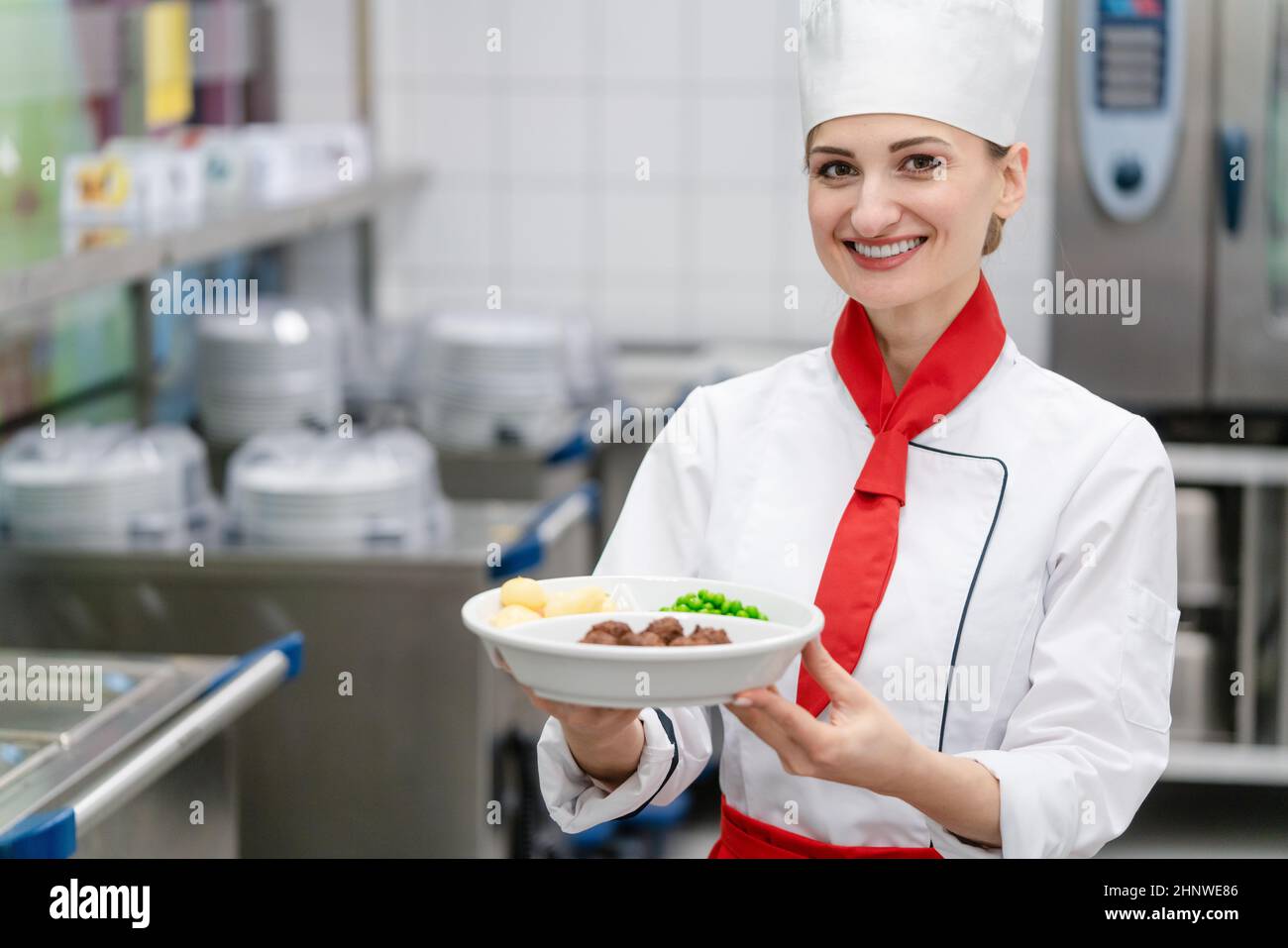 Proud cook showing plate with food in commercial kitchen of canteen ...