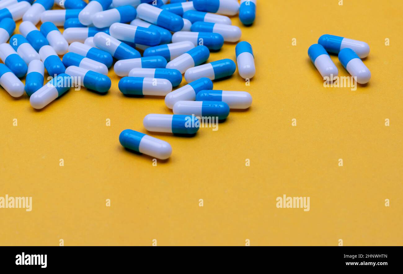 Blue and white antibiotic capsule pills spread on yellow background ...