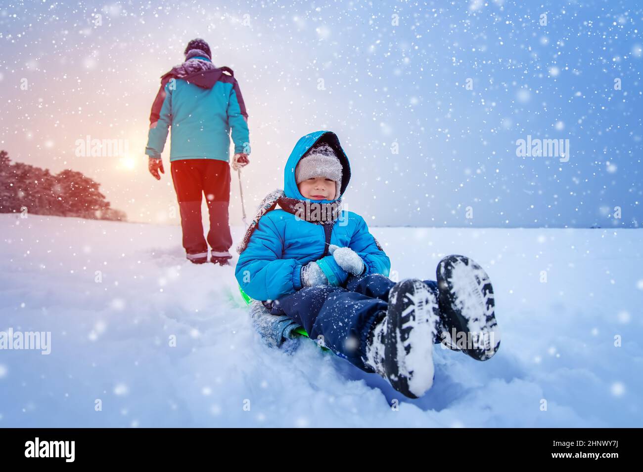 Father pulling sled with his lovely smiling son in snowfall. Concept of ...