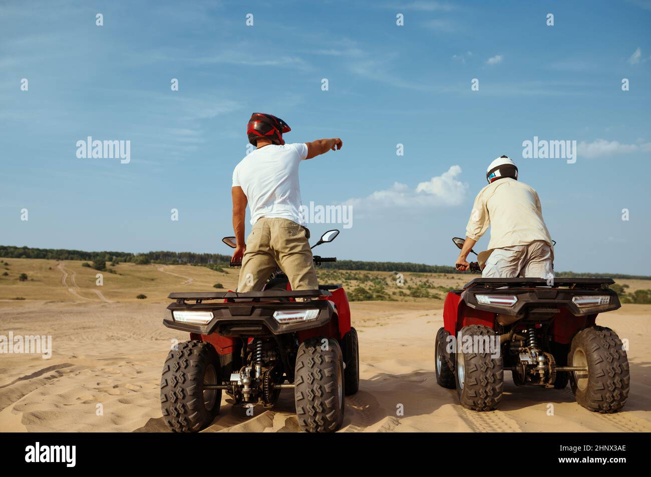 Two men in helmets ride on atv in desert, back view. Male persons on ...