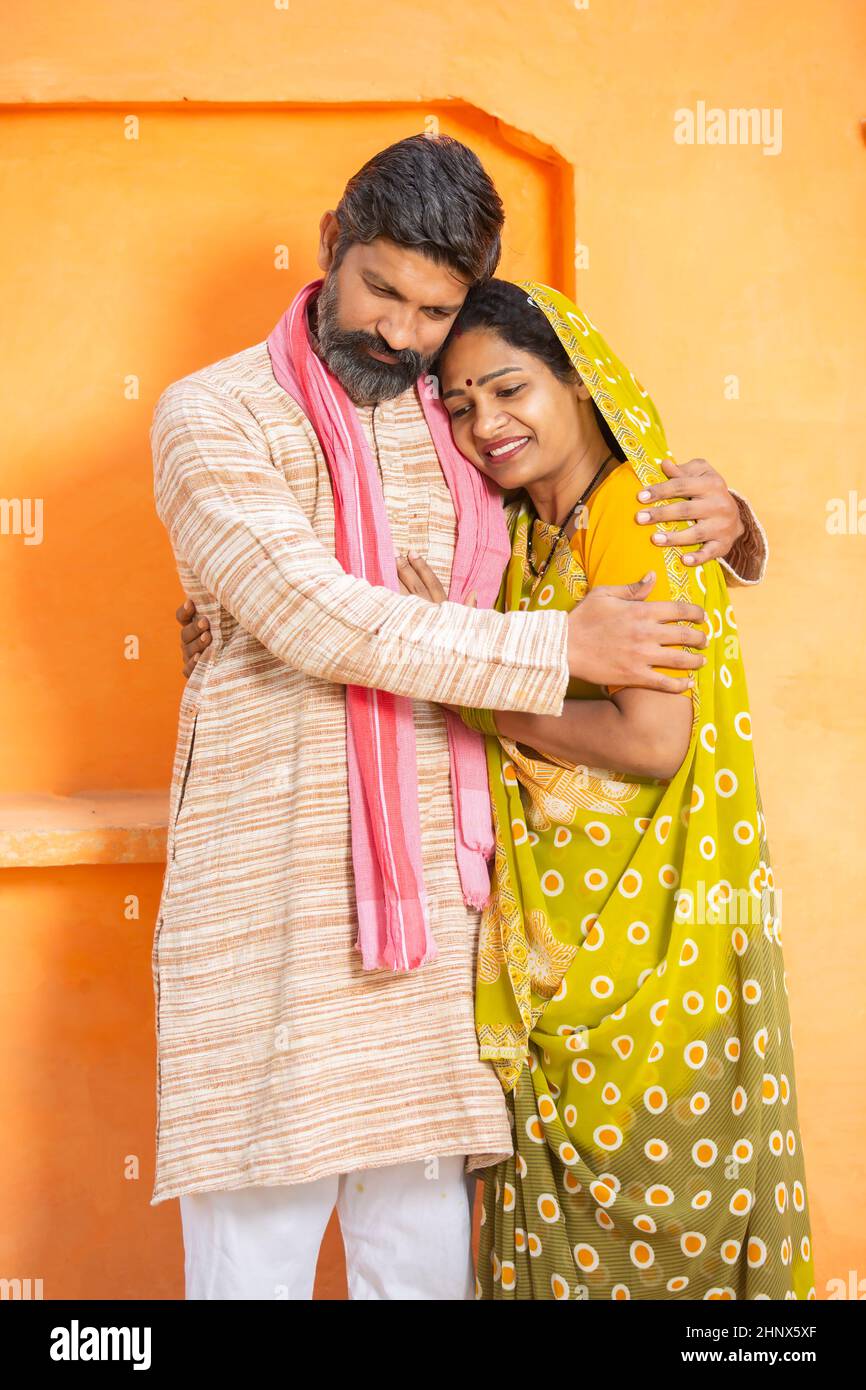 Rural indian couple hugging against orange background. man wearing ...