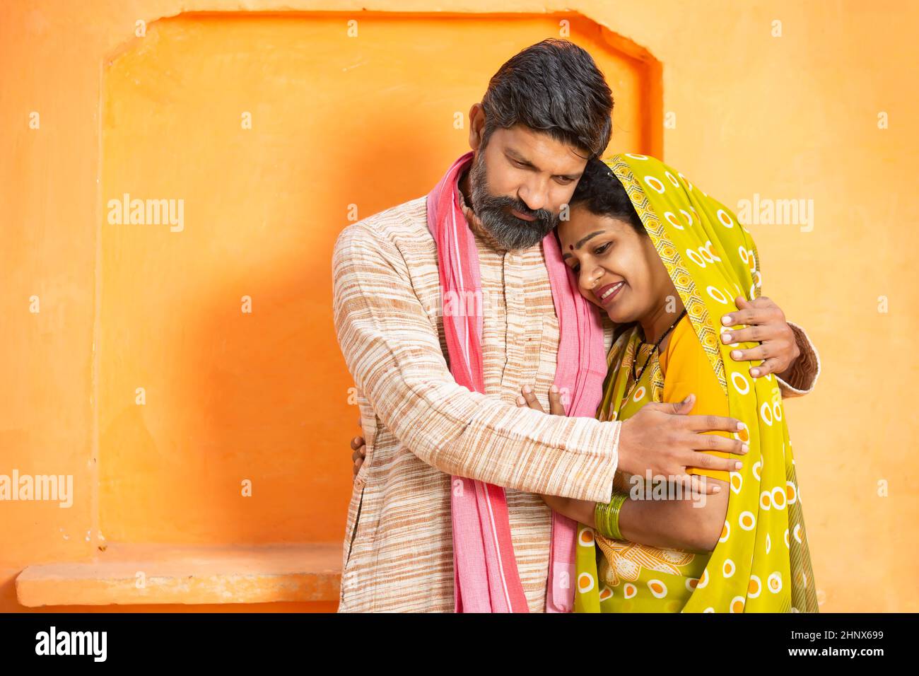 Rural indian couple hugging against orange background. man wearing ...