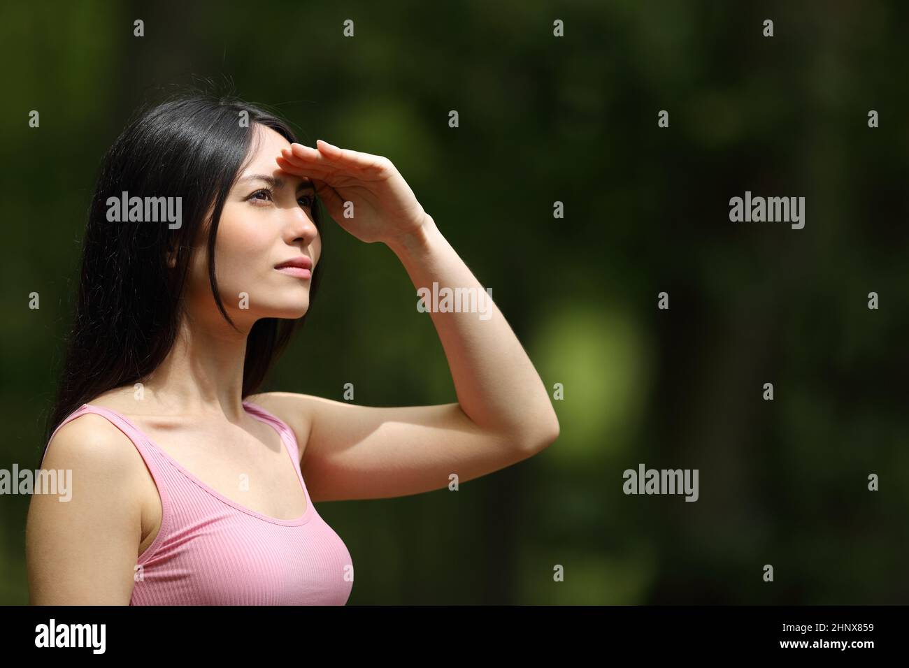 Concentrated asian woman protecting from sun with her hand searching in ...