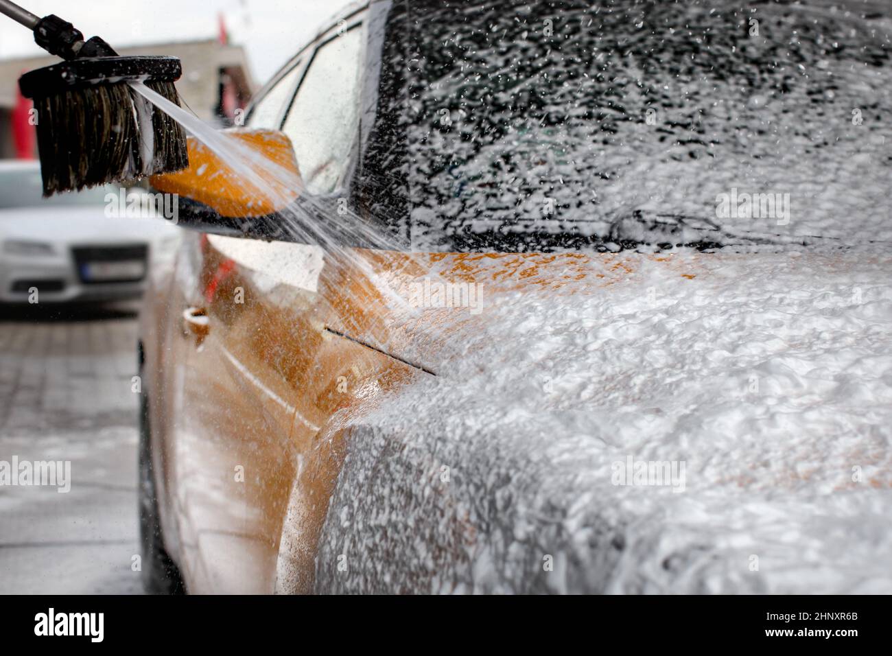 Water and shampoo stream falling on car covered with thick foam, when ...