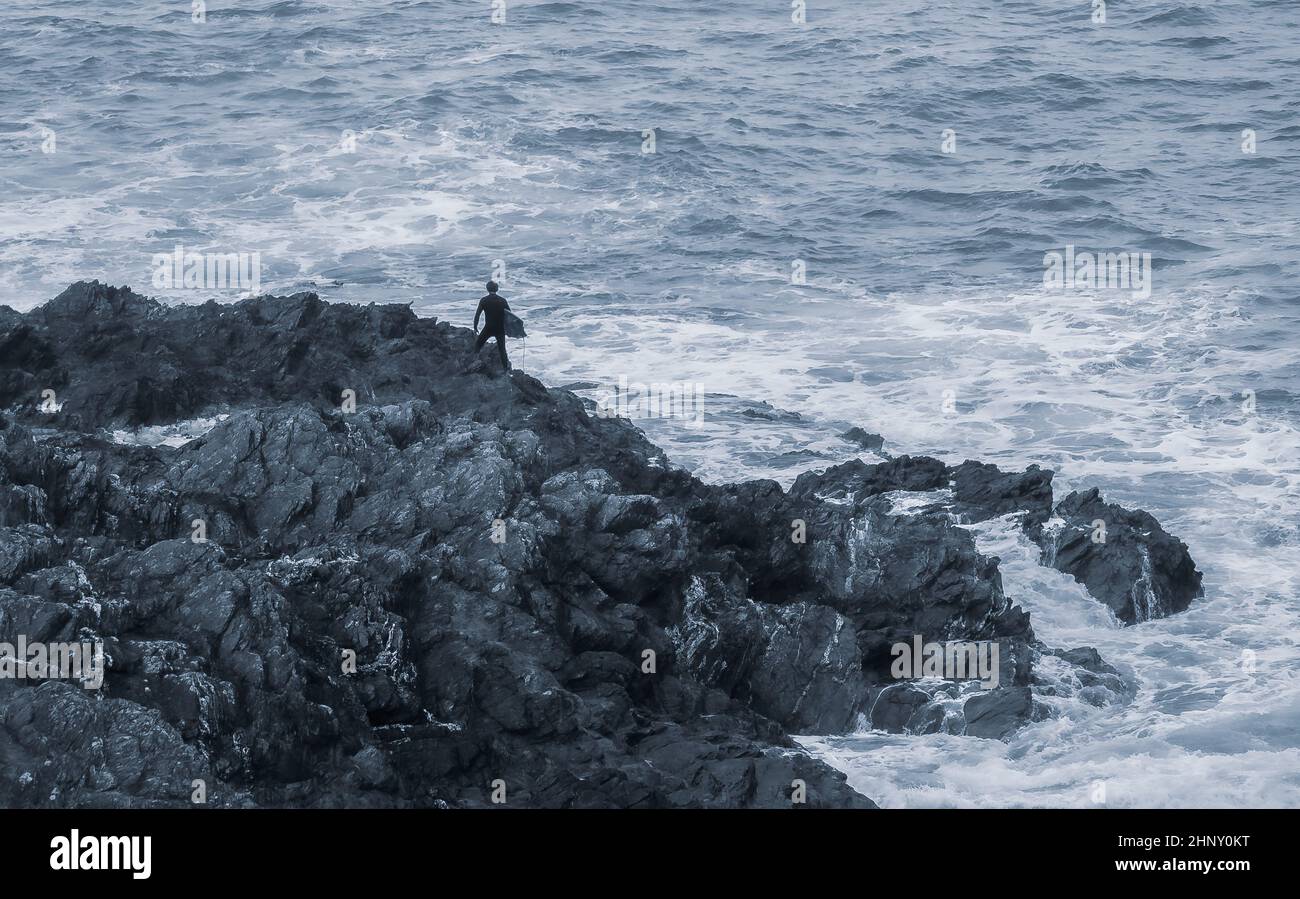 Male surfer carrying a surfboard on a rocky beach in Newquay Cornwall ...