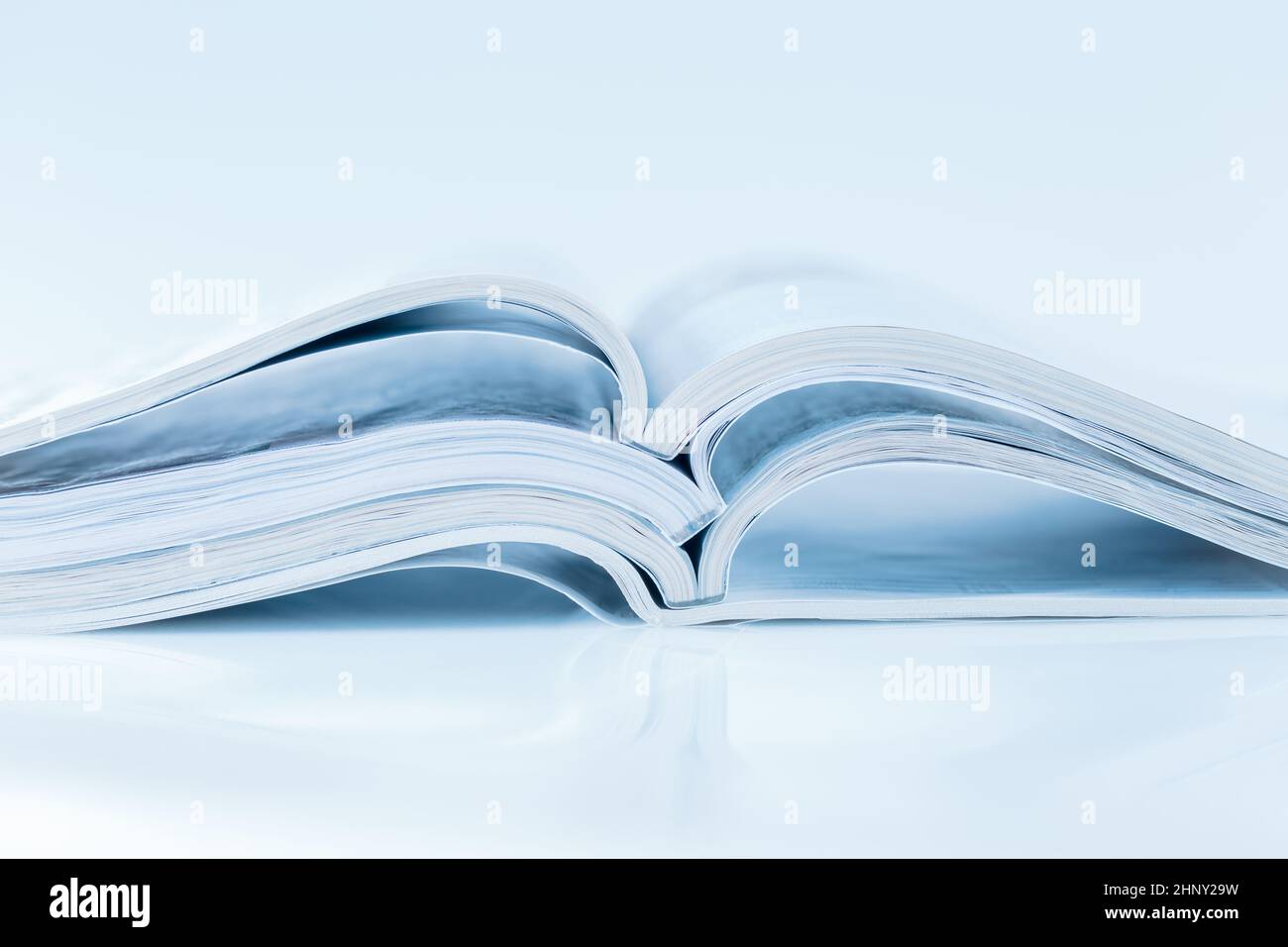 Stack of open magazines in blue tone on white background with copy ...