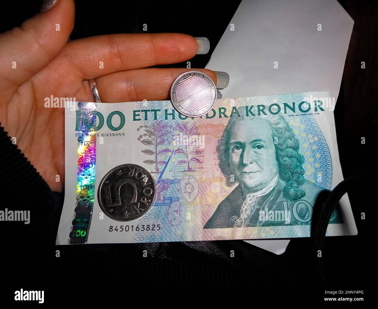 Swedish currency hundreds of notes and coins in hand. Dark background ...