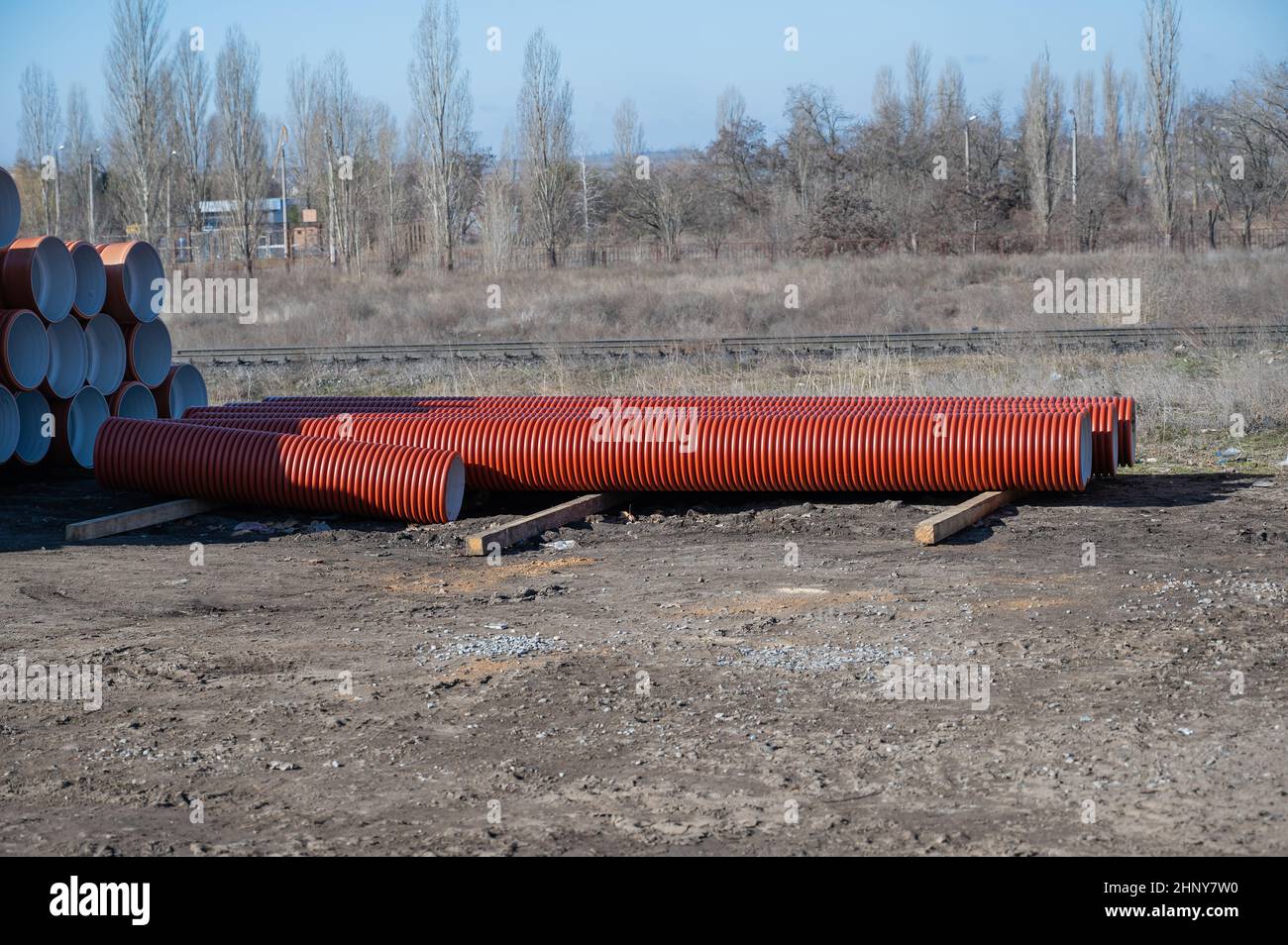Stack of new orange polypropylene pipes in front of the railroad ...