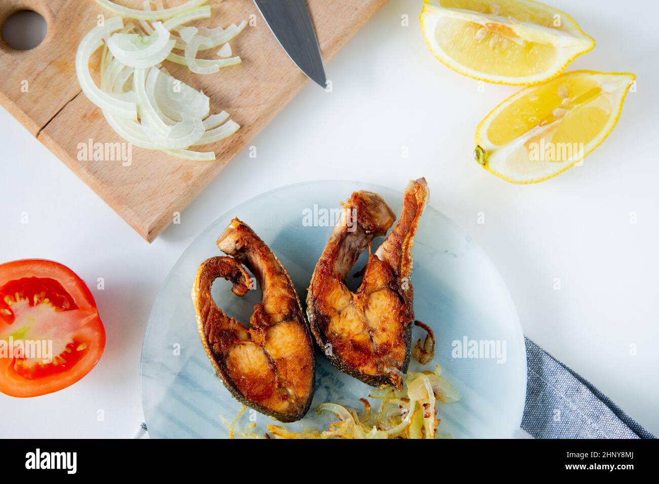 Fried fish with onions is on a plate, on a waffle towel, next to it is ...