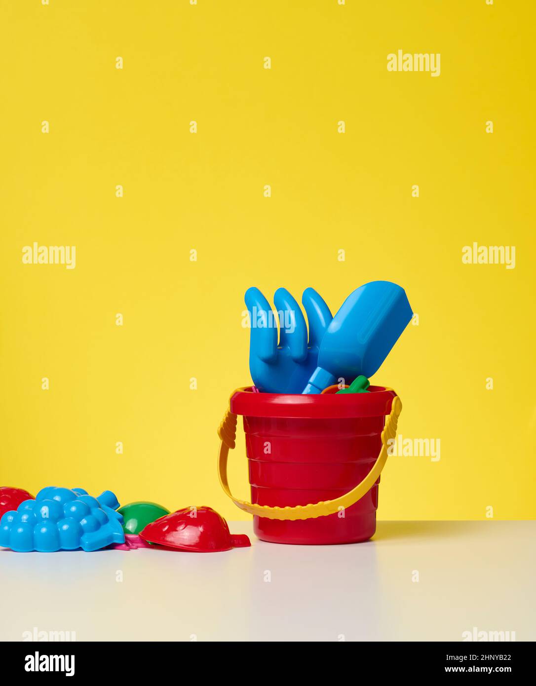 baby red plastic bucket with shovel and toys on a yellow background ...