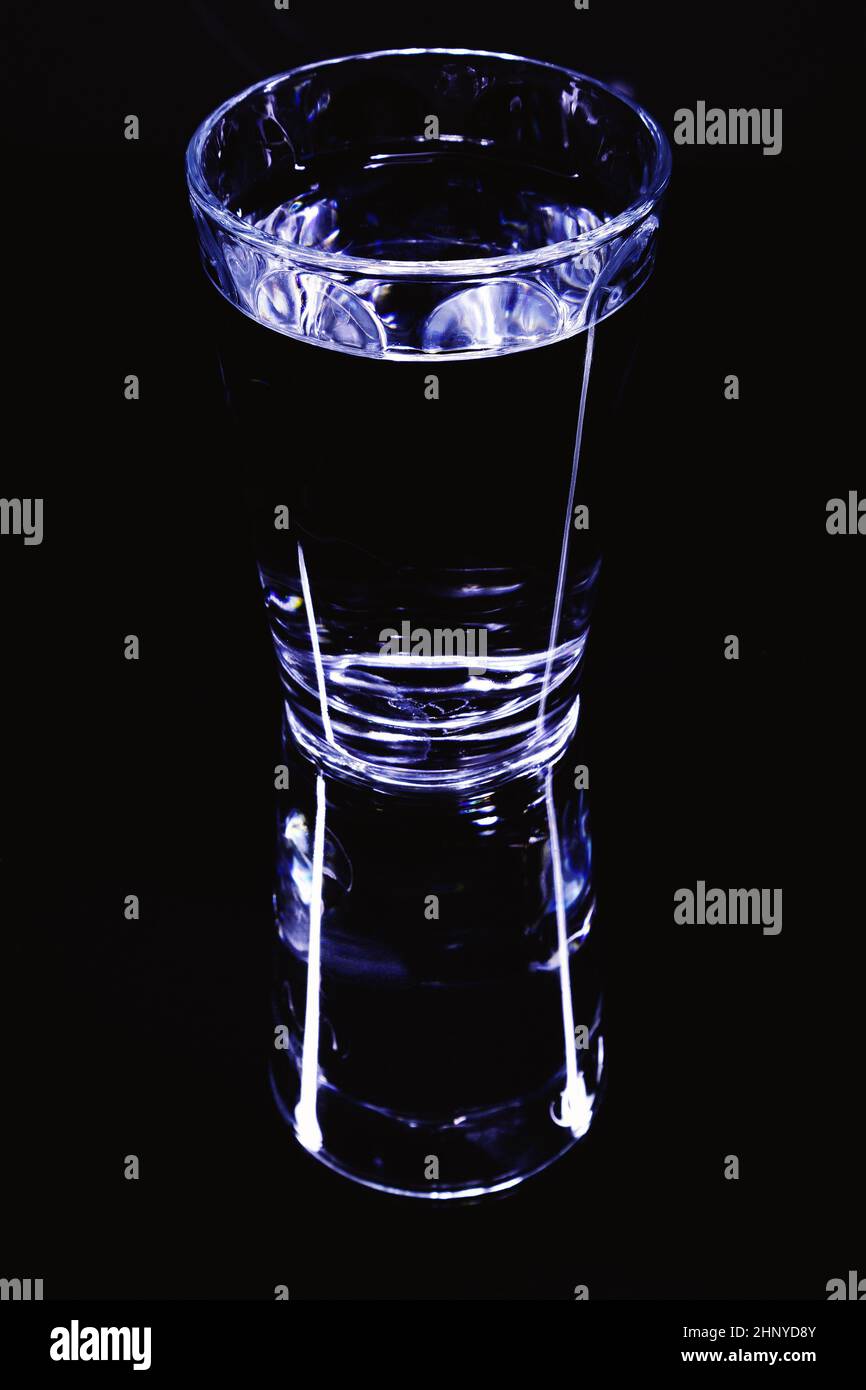 One glass of water on mirror in dark, accentuated shapes with highlight ...