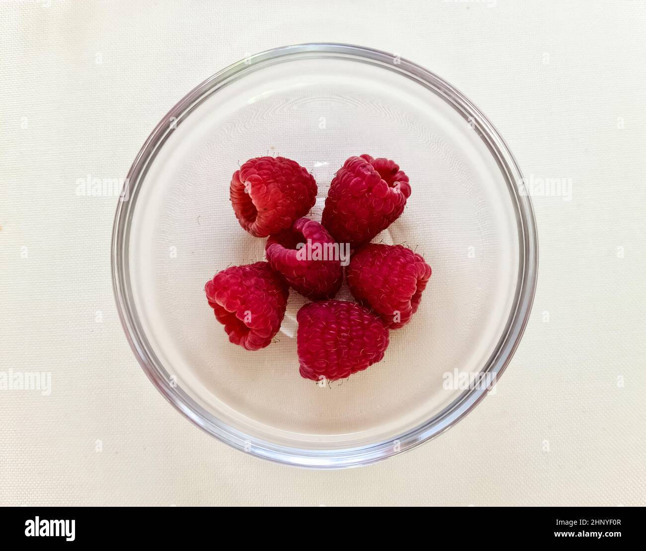 Six raspberries in a small glass bowl on a white table - top view Stock ...
