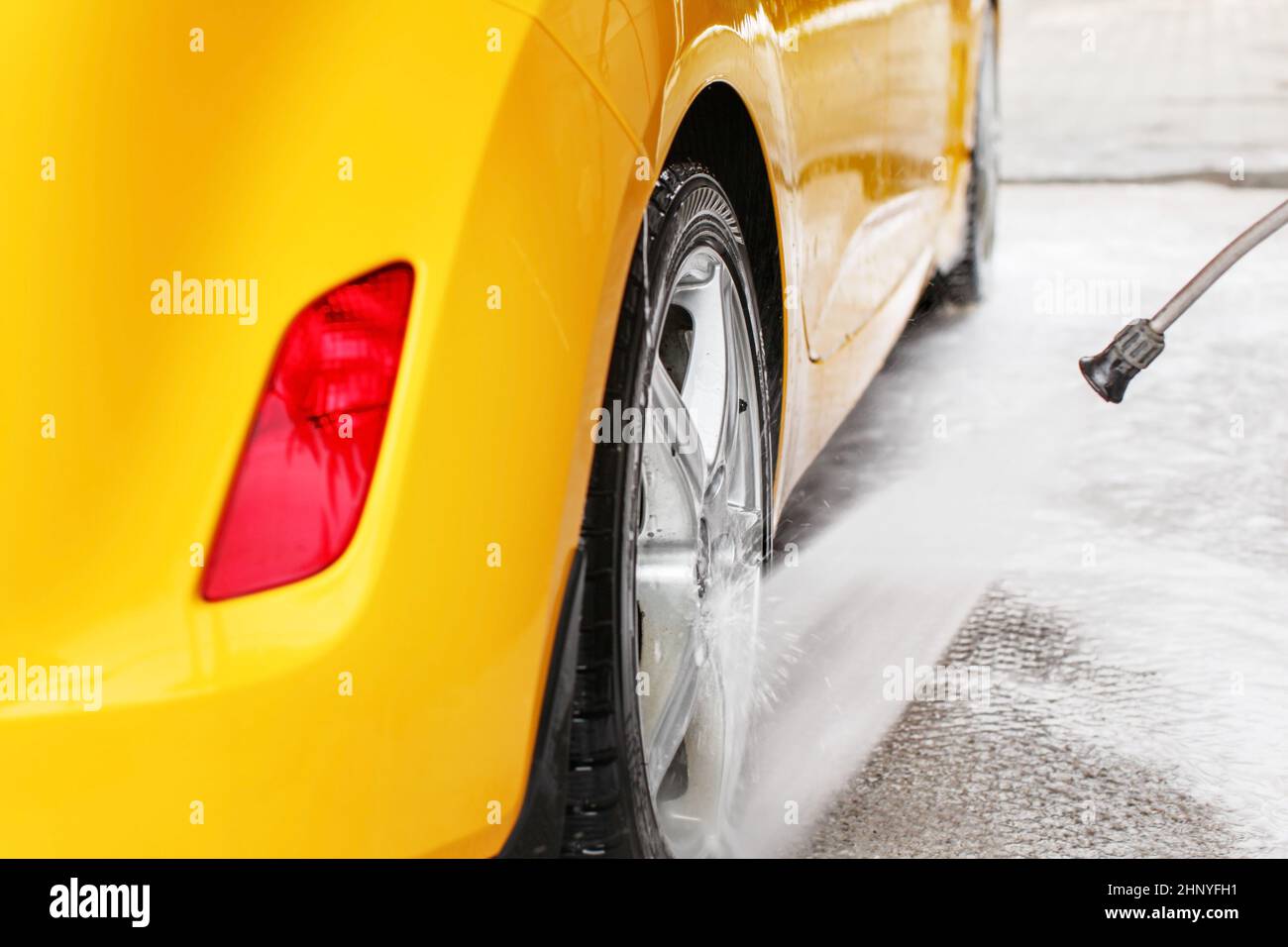 Rear wheel of yellow car being washed with jet water stream in carwash ...