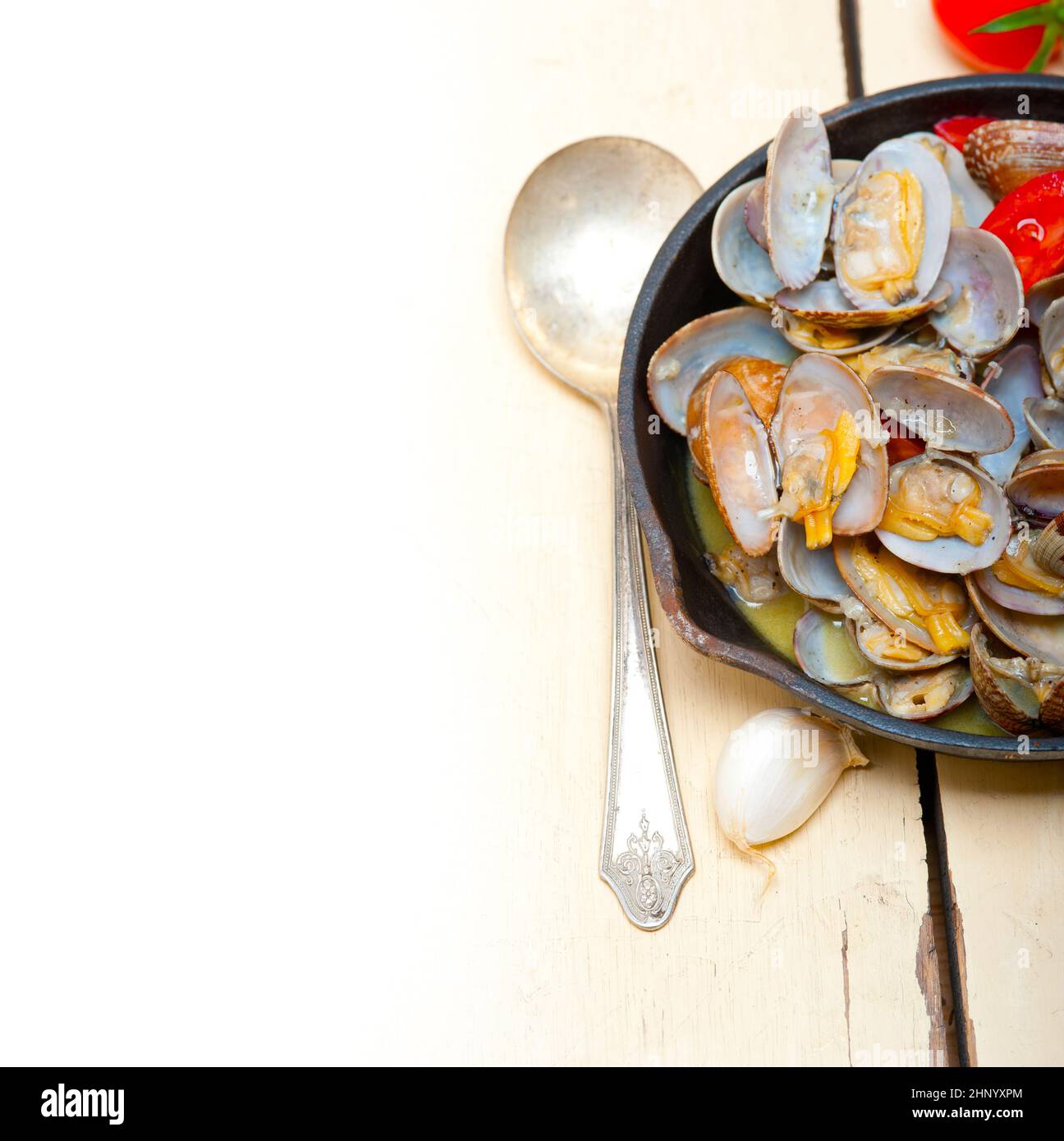 fresh clams stewed on an iron skillet over wite rustic wood table Stock ...