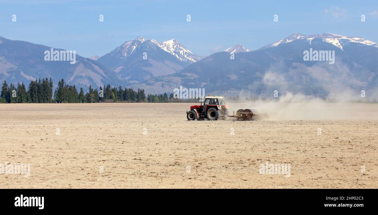 Tractor pulling rollers over dry fields in spring, mountains with ...