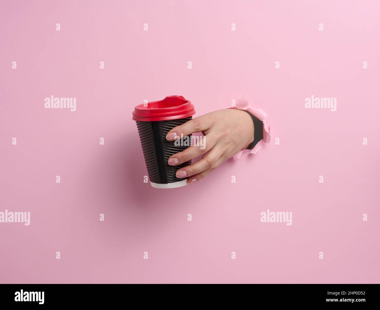 hand holds paper cardboard brown cup for coffee, pink background. Eco ...