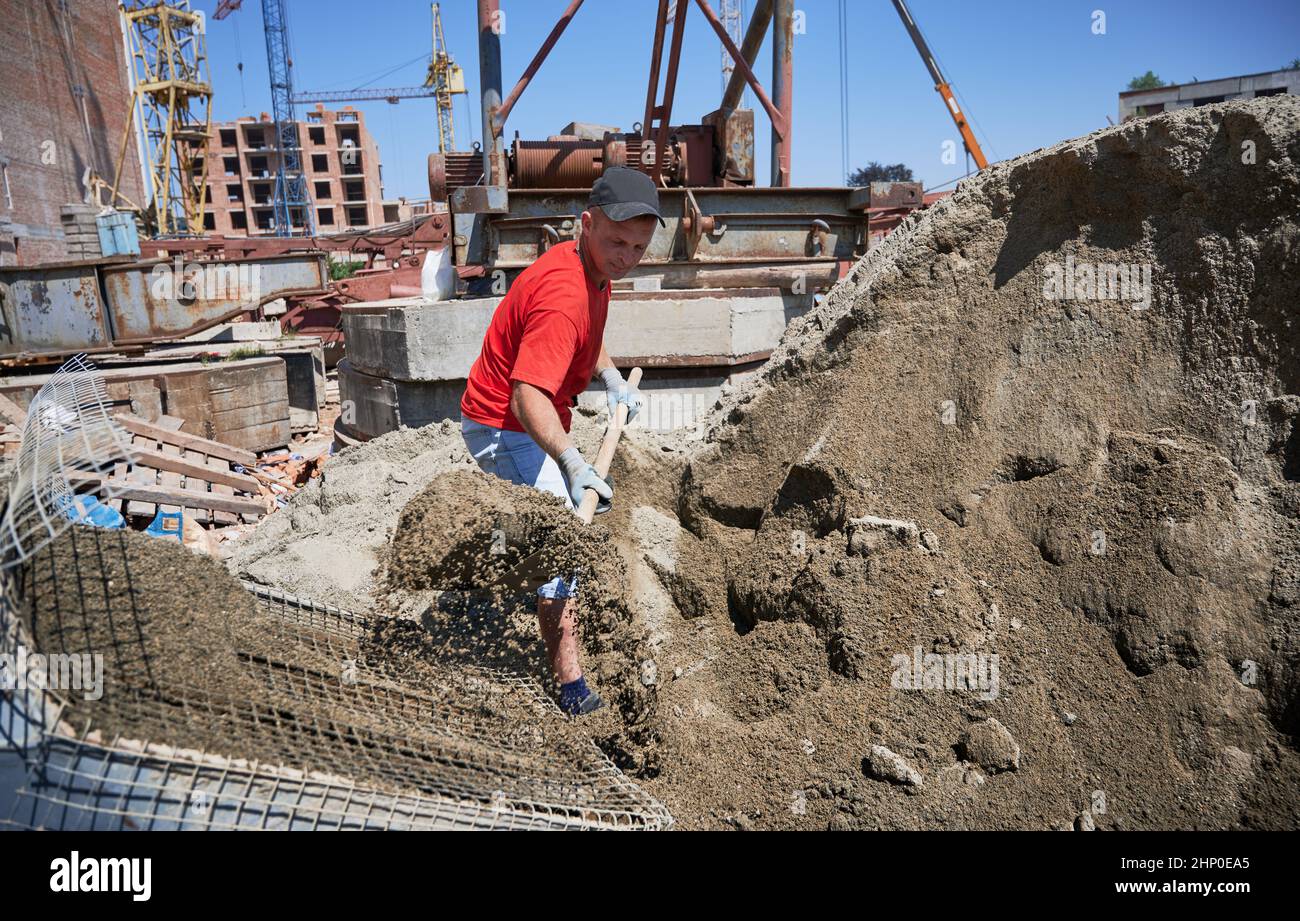 Male worker with shovel in his hands throwing cementitious floor screed ...