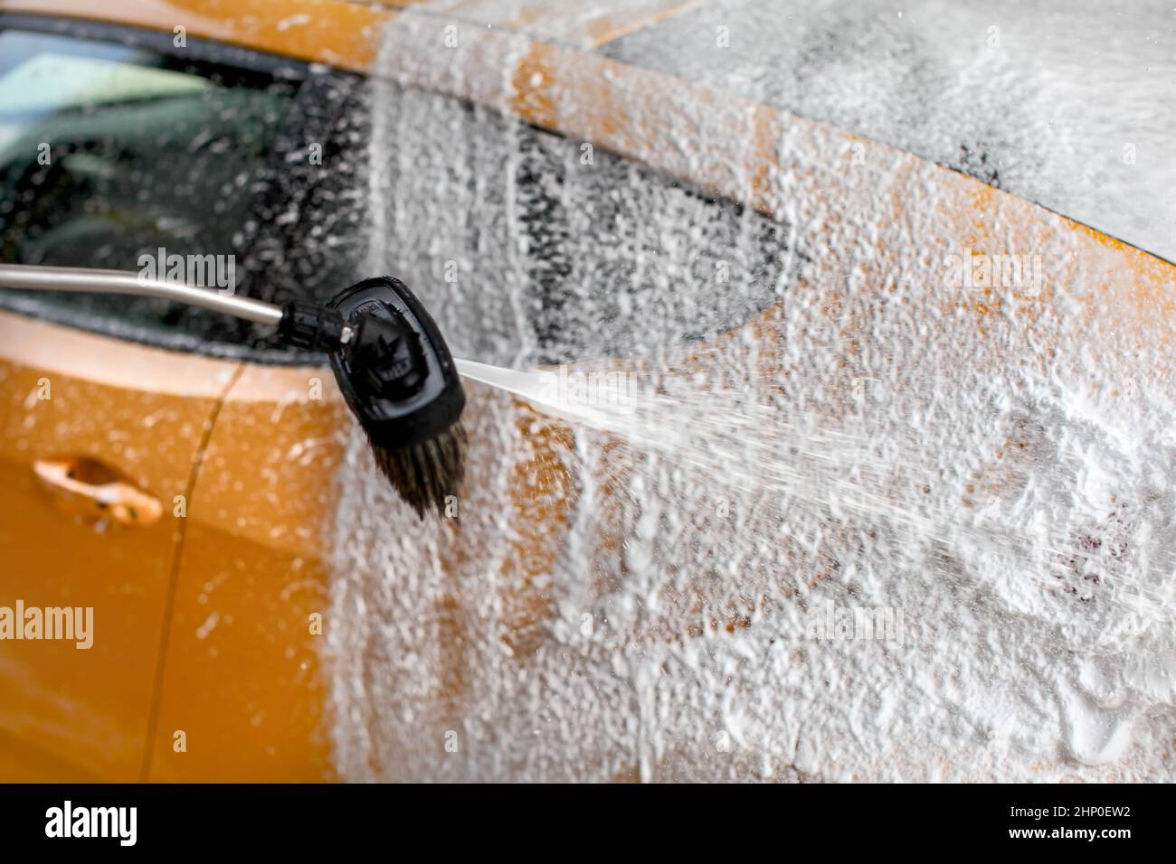Shampoo and foam being sprayed on yellow car side, cleaned at carwash ...