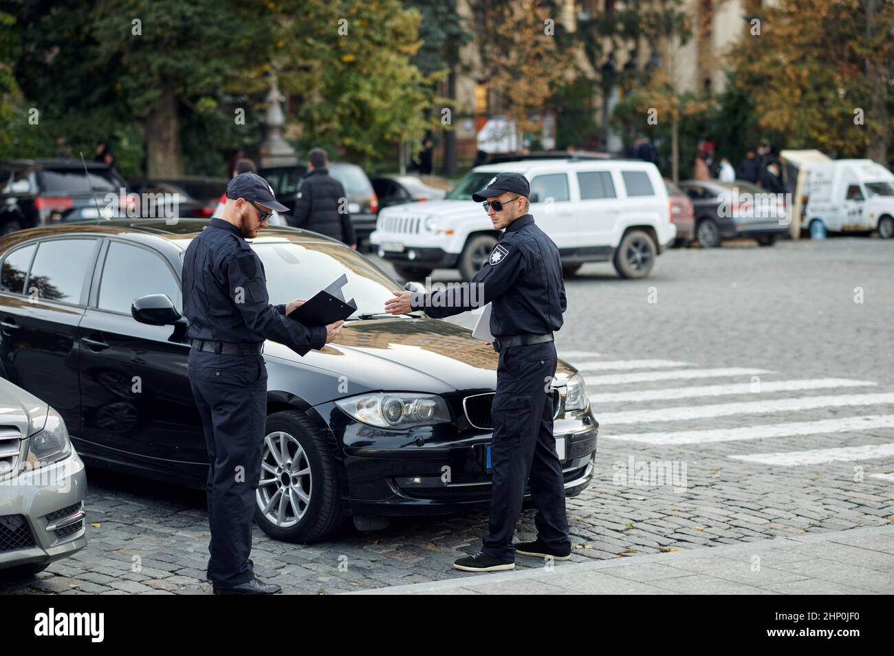 Two male police officers checking vehicle on car parking. Policemen in ...