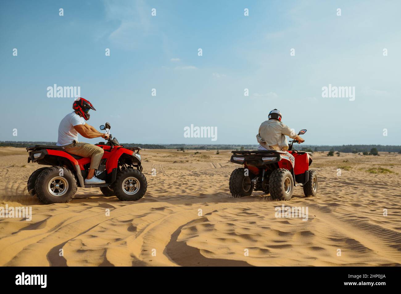 Two men in helmets riding on atv in desert sands, back view. Male ...