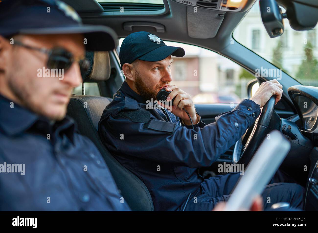 Two male police officers in uniform poses in the car. Policemen protect ...