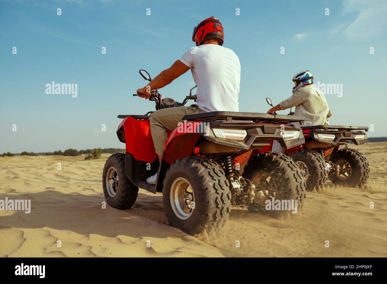 Two men in helmets riding on atv in desert sands, back view. Male ...