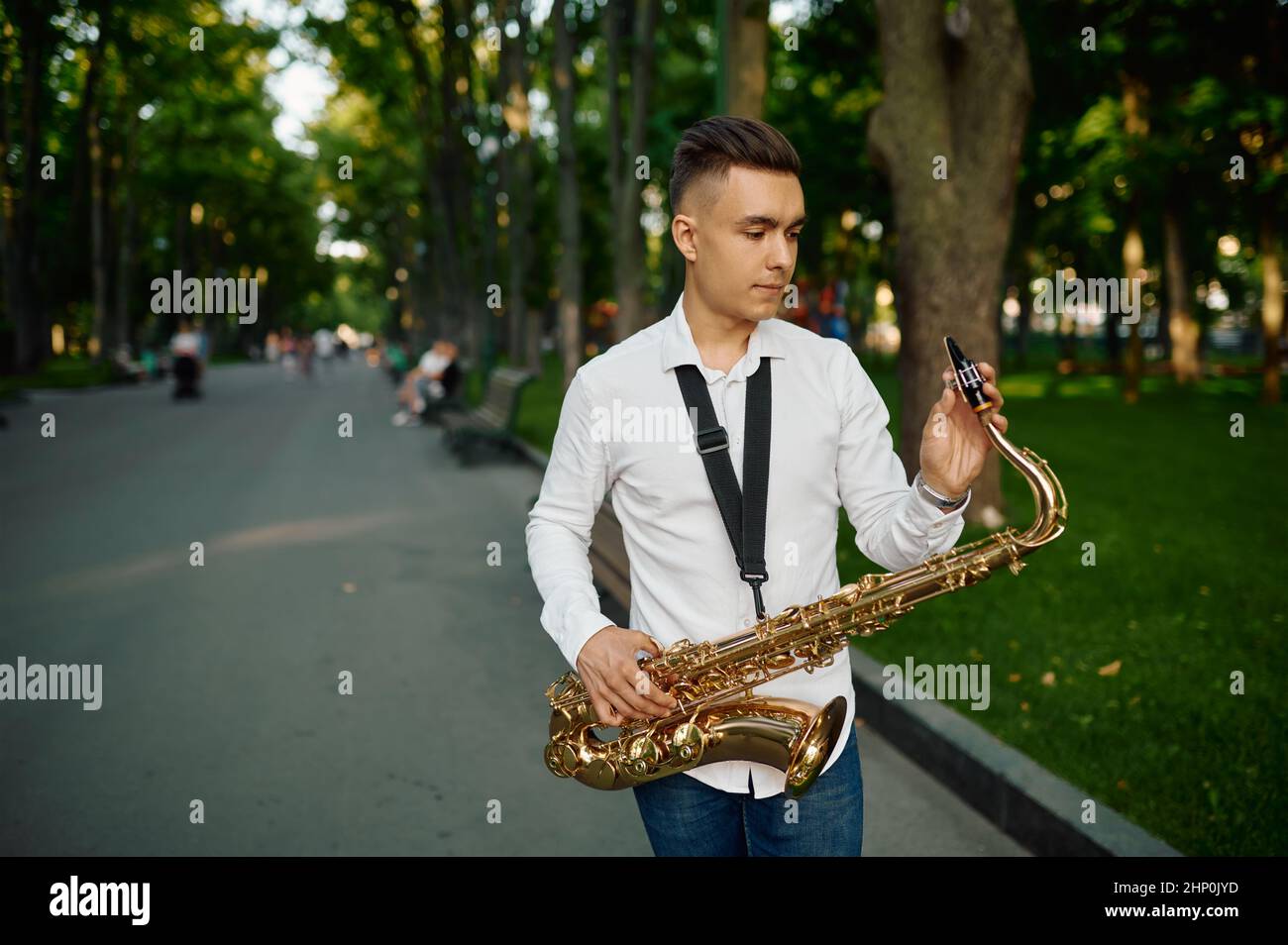 Young saxophonist with saxophone on the alley in summer park. Musician ...