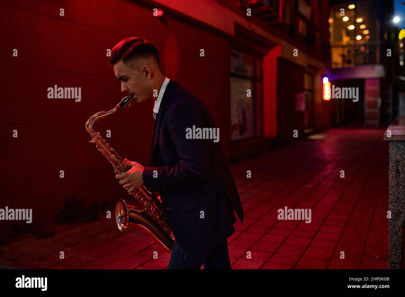 Young saxophonist plays the sax on the street at night, urban talent ...