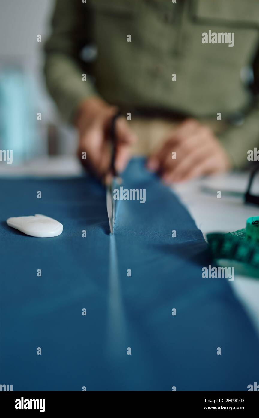 Dressmaker with scissors cuts cloth pattern at her workplace in ...