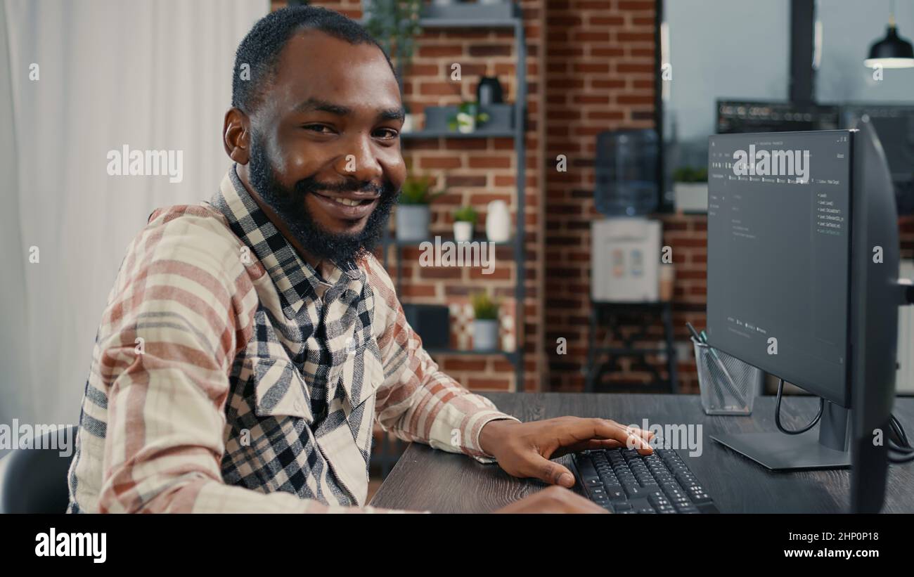 Software developer typing programming code on computer keyboard turning head and smiling while ...