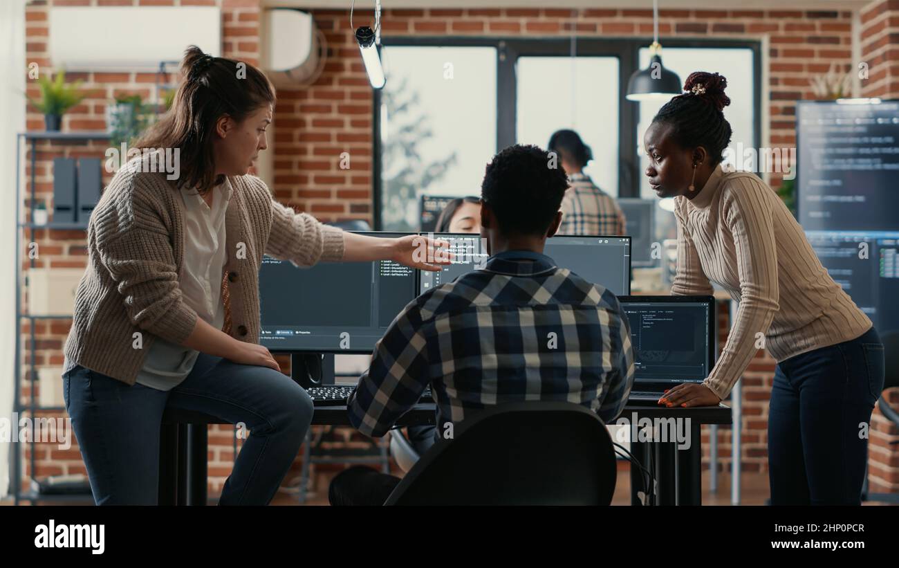 System engineer sitting on desk discussing with mixed team of coders ...