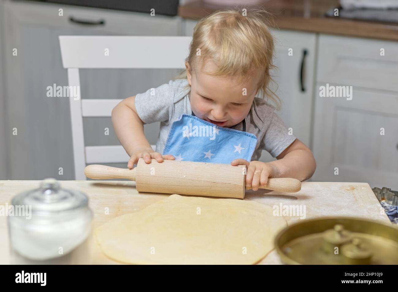 Little helper boy is rolling dough with a wooden rolling pin in ...