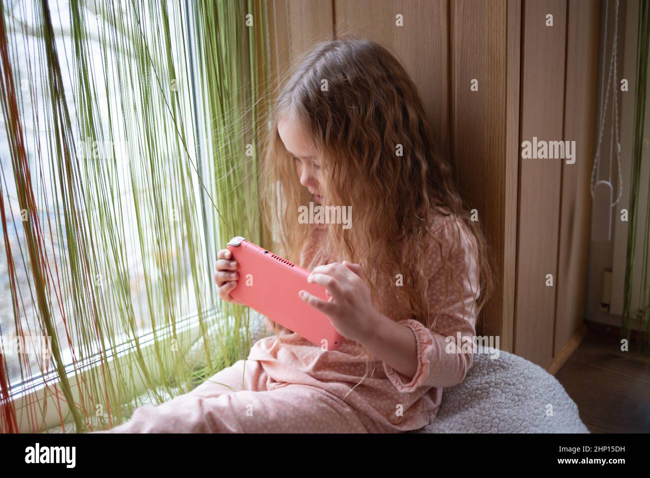 little cute girl plays a game console sitting on the windowsill Stock ...