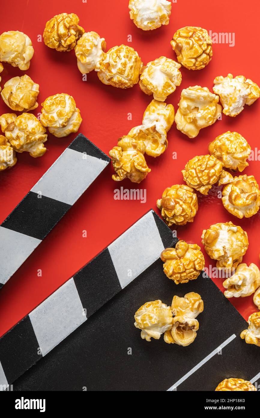 Sweet caramel popcorn and clapper board on red background. Top view ...