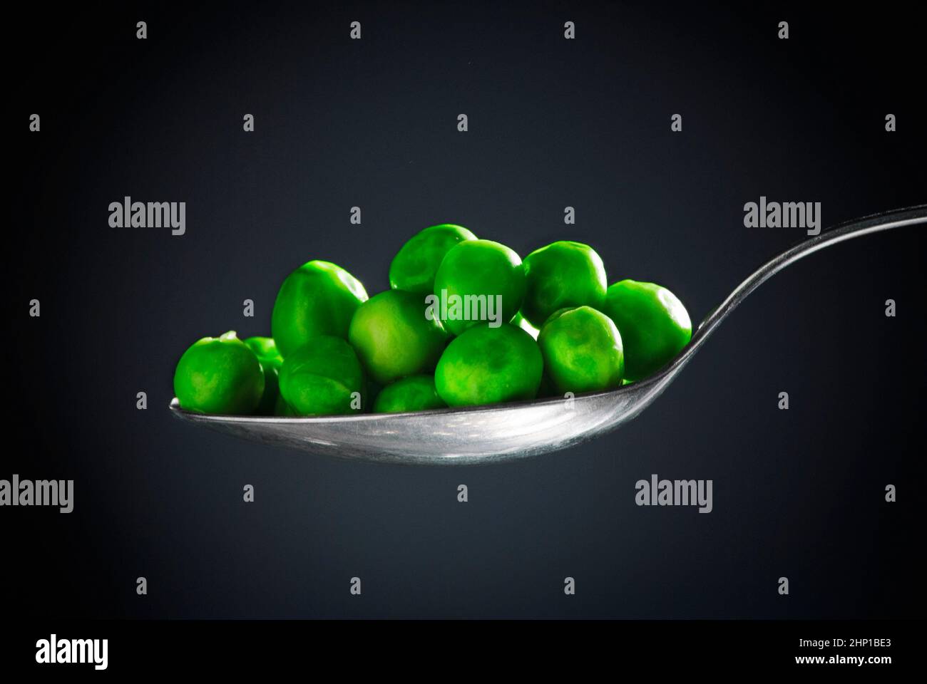 Spoon full of peas in front of black background Stock Photo - Alamy