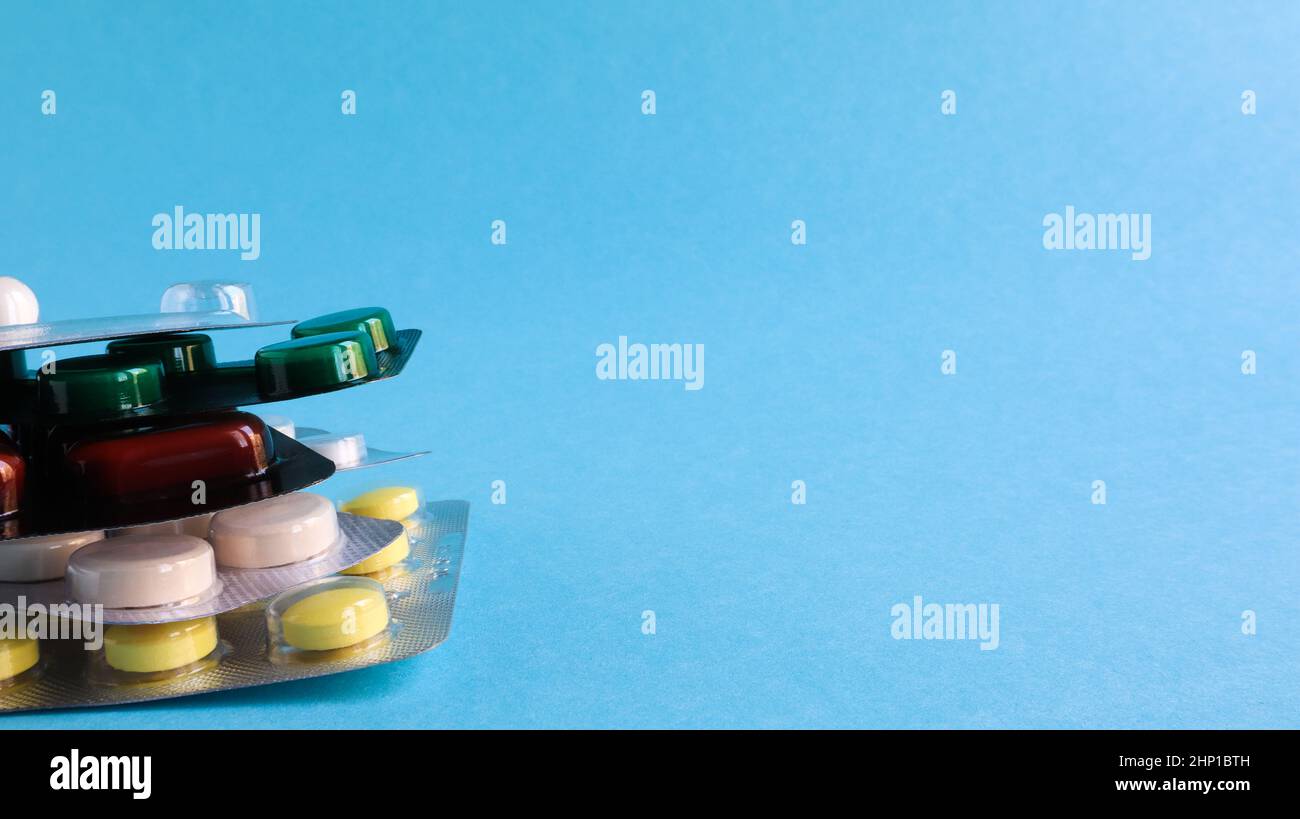 Packs of pills of various shapes and colors are stacked on a blue ...