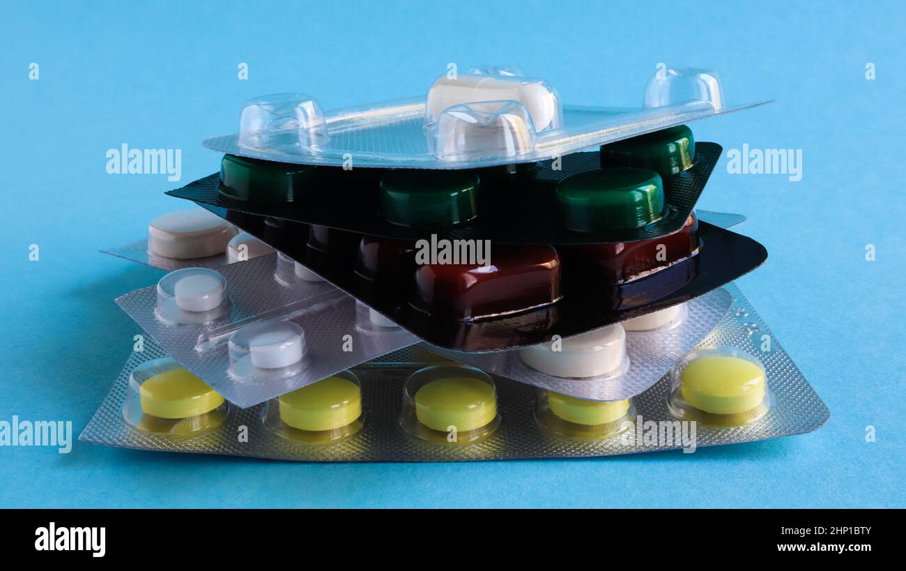 Packs of pills of various shapes and colors are stacked on a blue ...