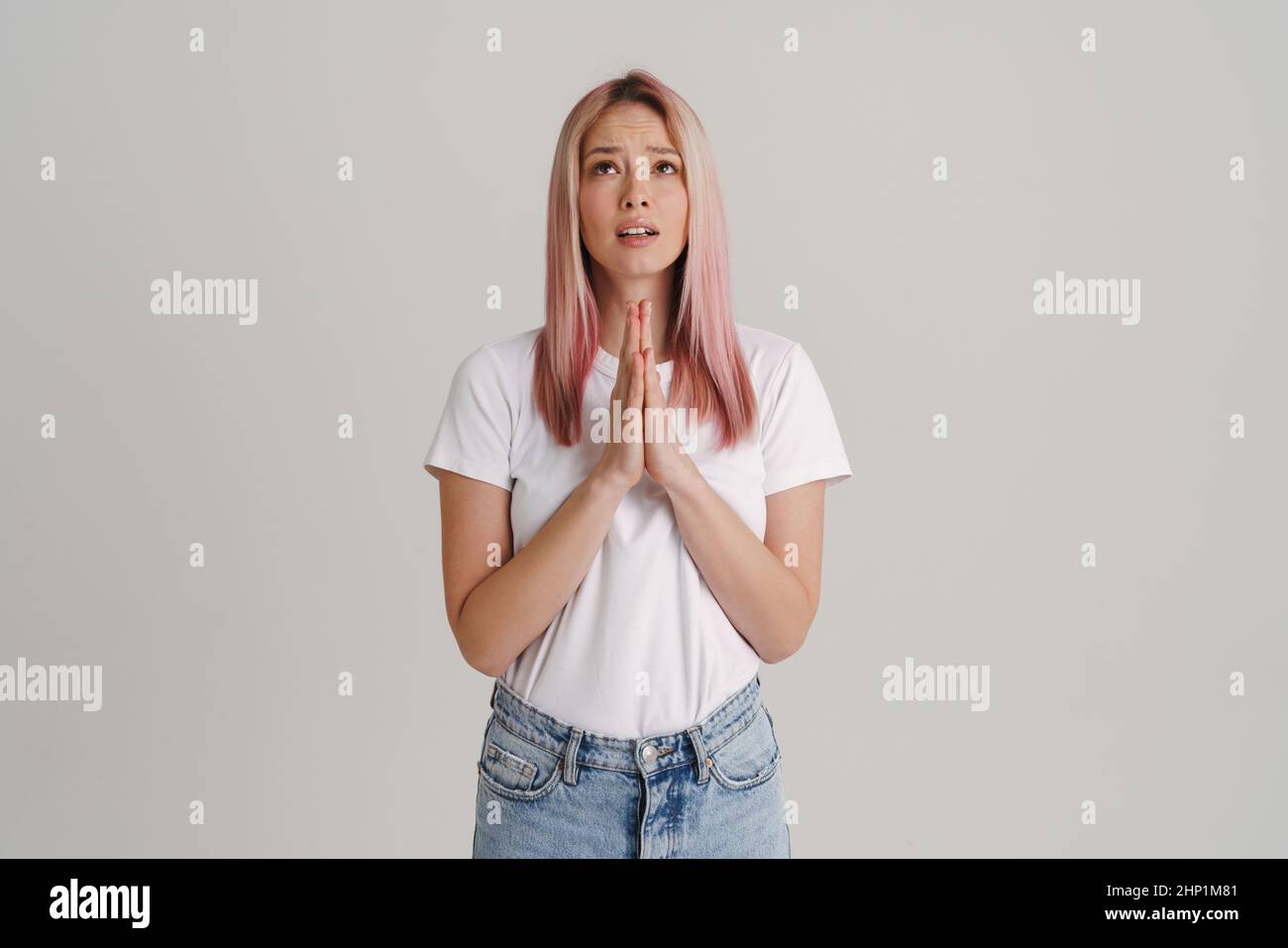 Young woman with pink hair frowning while holding palms together ...