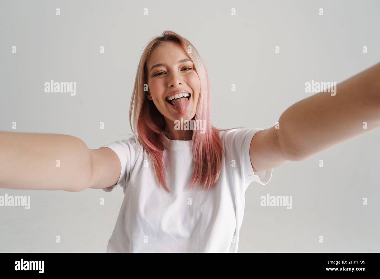 Young smiling woman showing er tongue while taking selfie photo ...