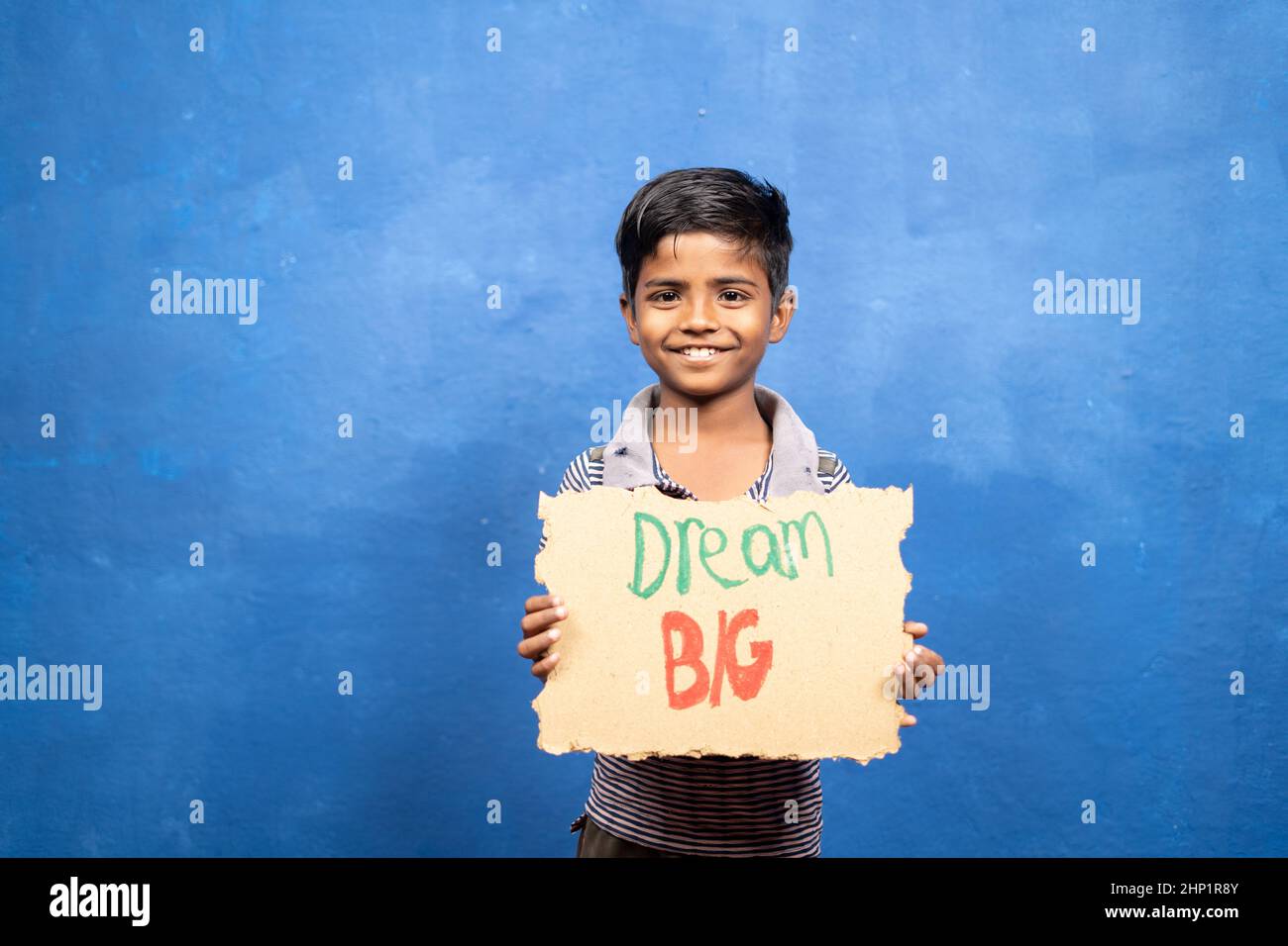 Happy smiling kid with dream big sign board standing against blue ...