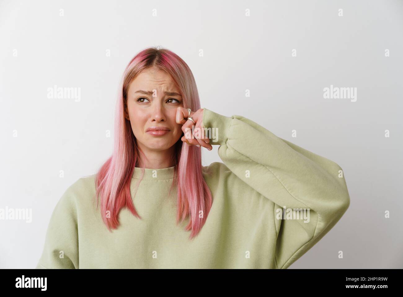 Young unhappy woman with pink hair crying and wiping her tears isolated ...