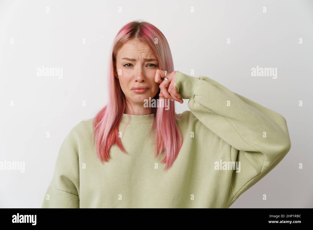 Young unhappy woman with pink hair crying and wiping her tears isolated ...