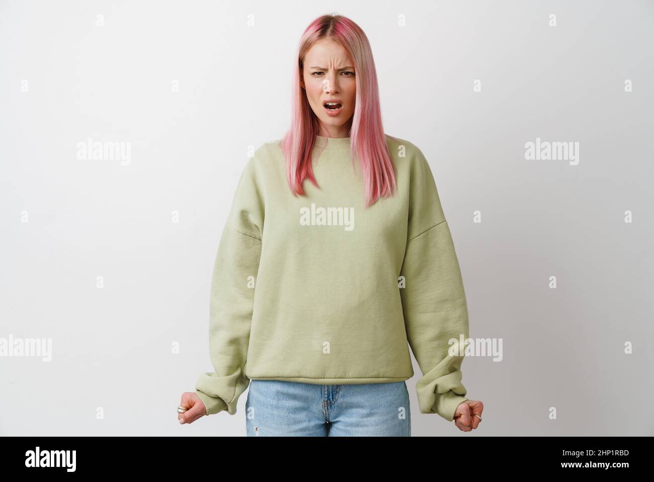 Young displeased woman with pink hair frowning and clenching her fists ...