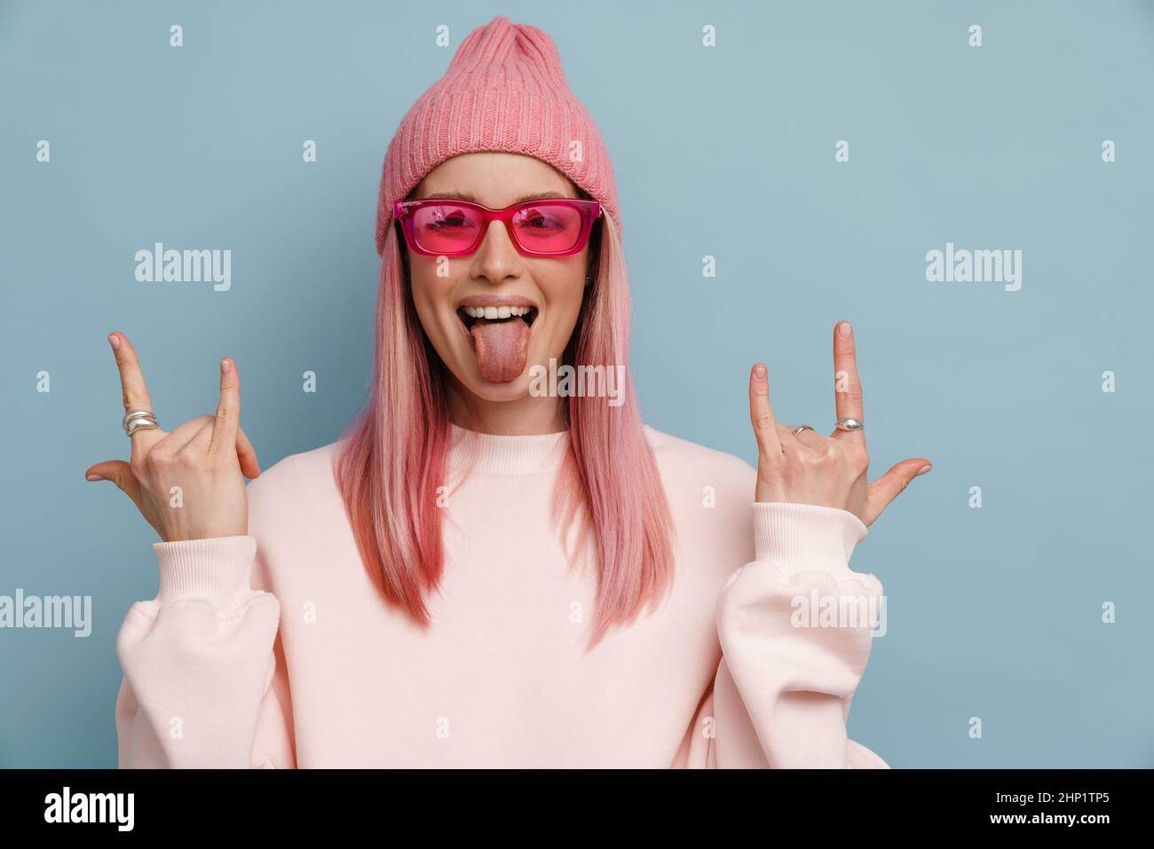 Young white woman gesturing horns sign and sticking out her tongue at ...